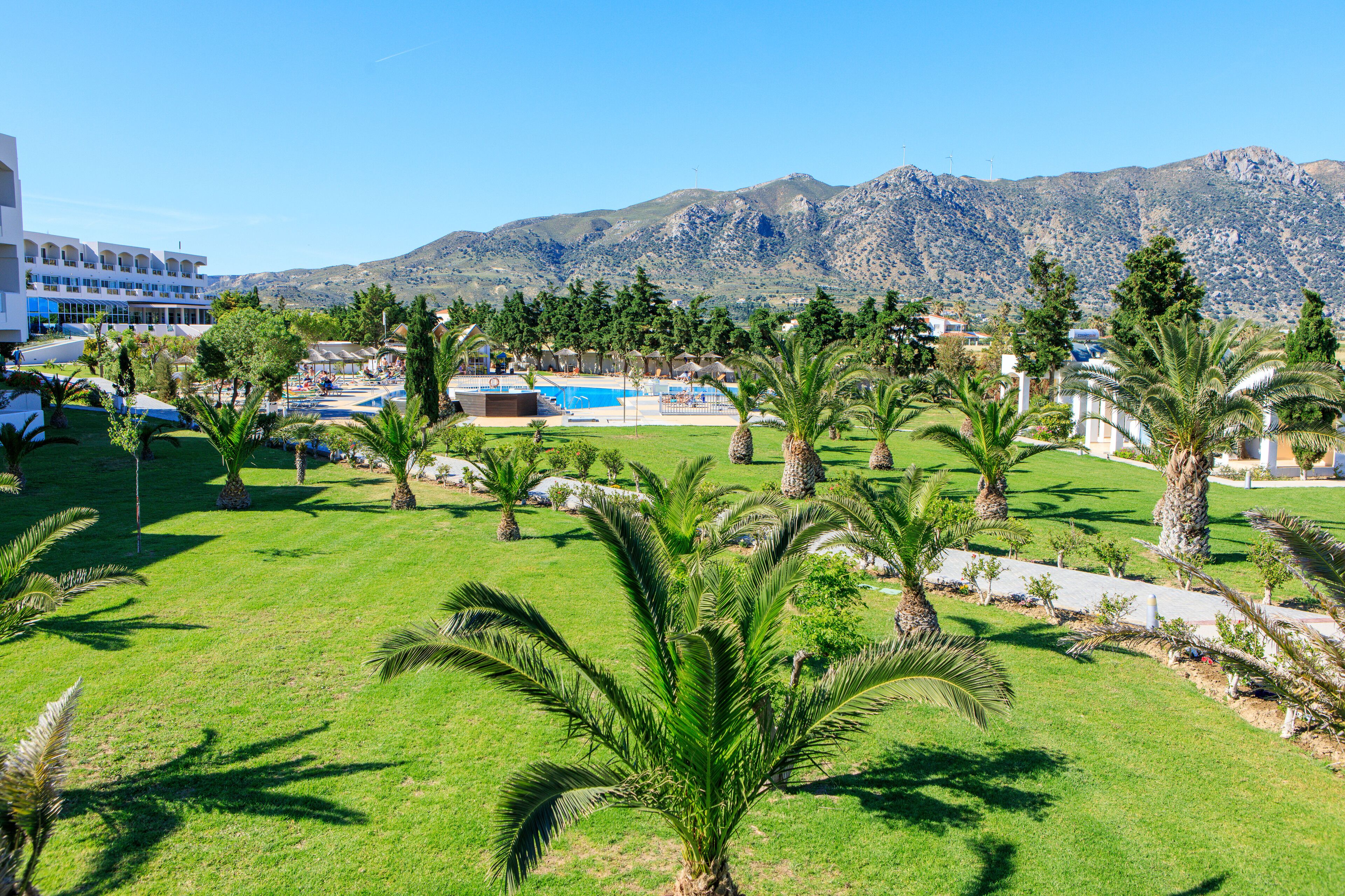Um resort com piscina, palmeiras e montanhas ao fundo.