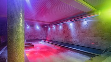 Uma área interna de piscina moderna, com piso ladrilhado, paredes de mármore e um elemento central de água.