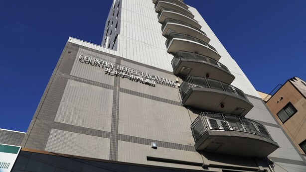 Um edifício alto com varandas e uma placa com a inscrição "SUNTORY HOTEL TAKAYAMA".