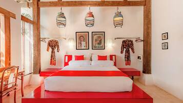 Quarto moderno com uma cama grande, vigas de madeira, gaiolas de pássaros penduradas e quadros nas paredes.