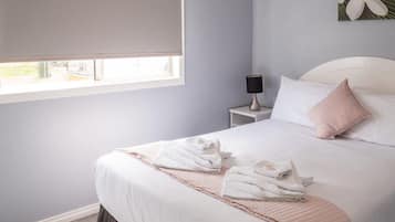 Cama bem arrumada com toalhas dobradas, abajur e janela com vista.