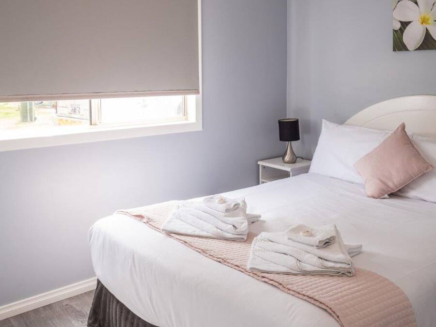 Cama bem arrumada com toalhas dobradas, abajur e janela com vista.