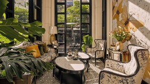 Um quarto aconchegante com sofá, poltronas, mesa de centro e plantas grandes.