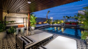 Uma área de piscina no terraço com espreguiçadeiras, espaço para sentar e vista para a cidade.