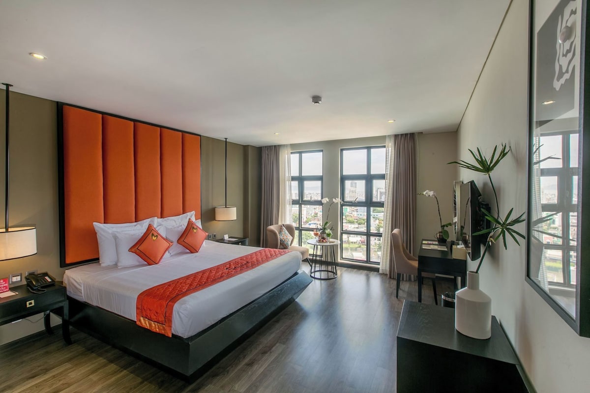Quarto de hotel moderno com uma cama grande, uma escrivaninha e vista para a cidade.