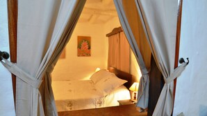Quarto com cama, cortinas, um quadro na parede e mesa de cabeceira com abajur.