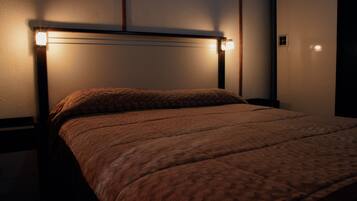 Cama bem arrumada com cabeceira, luminária fixada na parede e uma pequena janela.