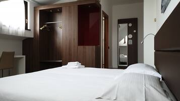 Quarto de hotel com cama, escrivaninha, guarda-roupa e espelho.