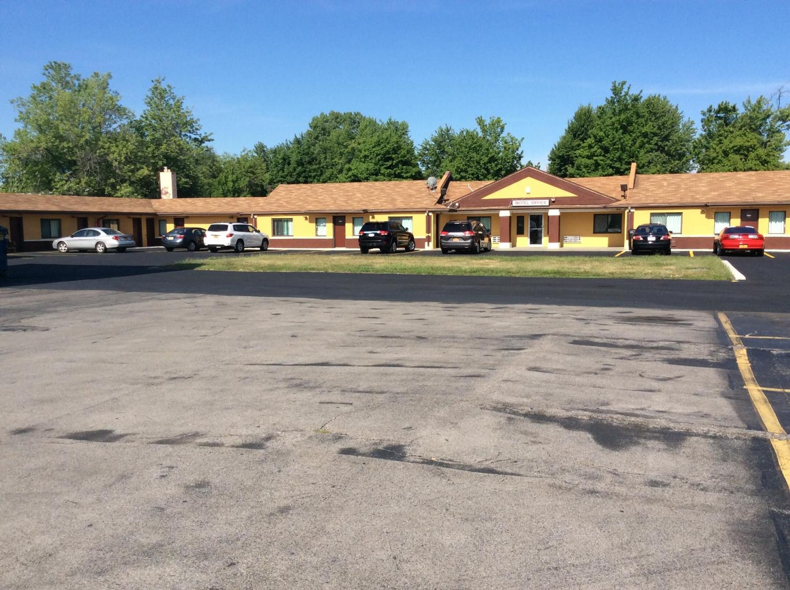 Um motel com estacionamento e vários carros estacionados na frente.