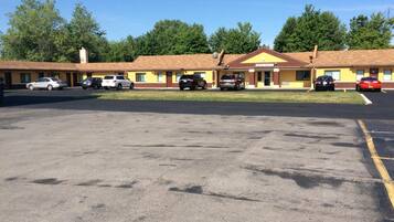 Um motel com estacionamento e vários carros estacionados na frente.