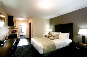 Quarto de hotel com cama, mesa de cabeceira, abajur e escrivaninha com cadeira.