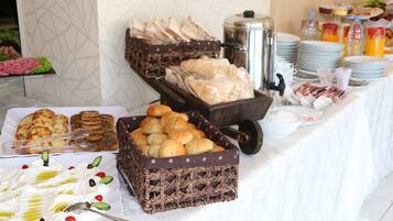 Mesa de buffet com diversos alimentos, incluindo pão, pastelaria e uma seleção de bebidas.