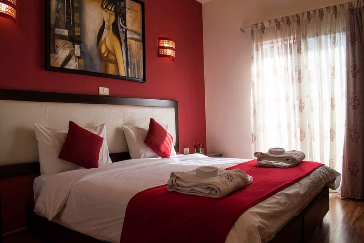 Quarto de hotel com uma cama grande, almofadas vermelhas, um cobertor vermelho e um quadro na parede.