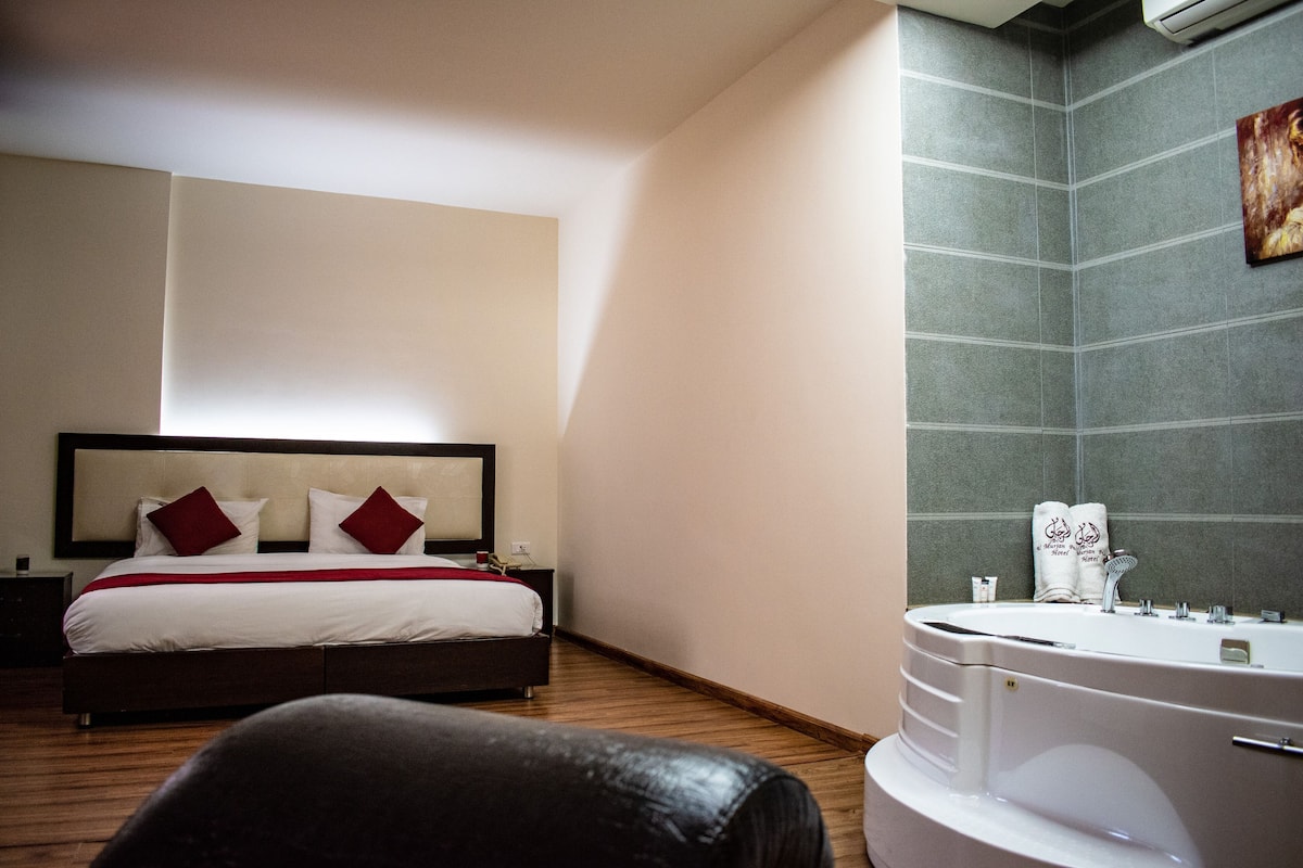 Quarto de hotel com cama, uma banheira grande e piso de madeira.