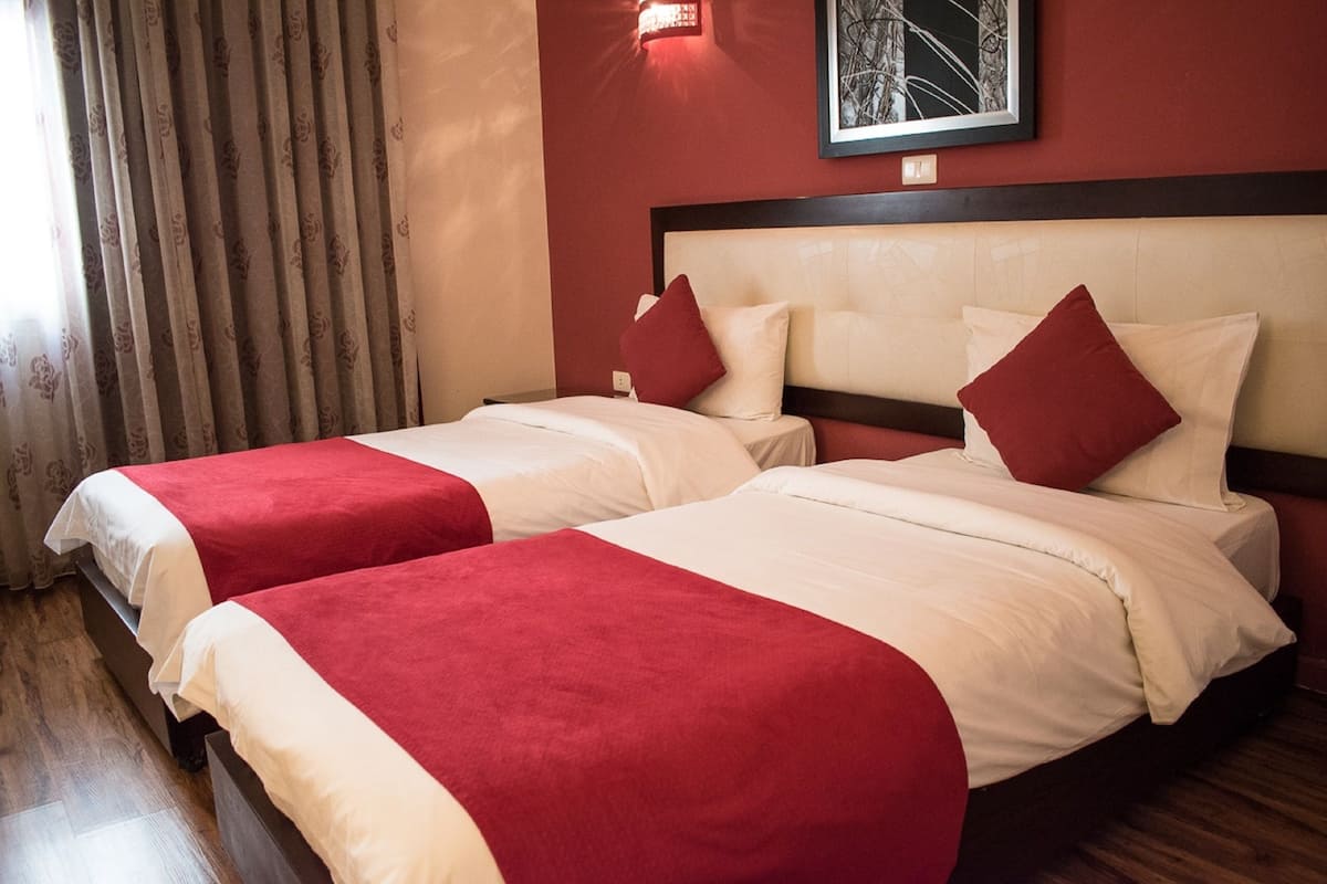 Quarto de hotel com duas camas, cada uma com roupa de cama vermelha e branca, cabeceira e um quadro na parede.