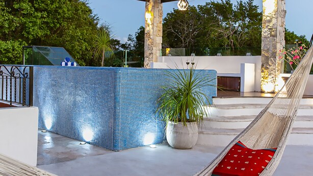 Uma rede sob um teto de vidro, área de piscina com azulejos azuis em mosaico e um pilar de pedra.