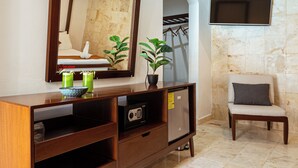 Uma casa de banho moderna com toucador de madeira, um espelho grande, uma planta em vaso e um espaço de estar com uma poltrona estofada.