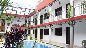 Um pátio com piscina, plantas em vasos e um edifício com varandas e colunas.