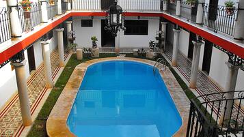 Piscina com deck vermelho, rodeada por um prédio branco com varandas e colunas.
