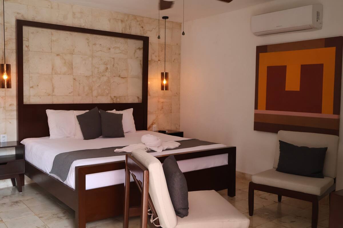 Quarto de hotel com uma cama grande, uma cadeira, uma escrivaninha e um ar condicionado.