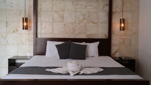 Cama bem arrumada com cabeceira escura, duas mesas de cabeceira e parede com padrão que lembra mármore.