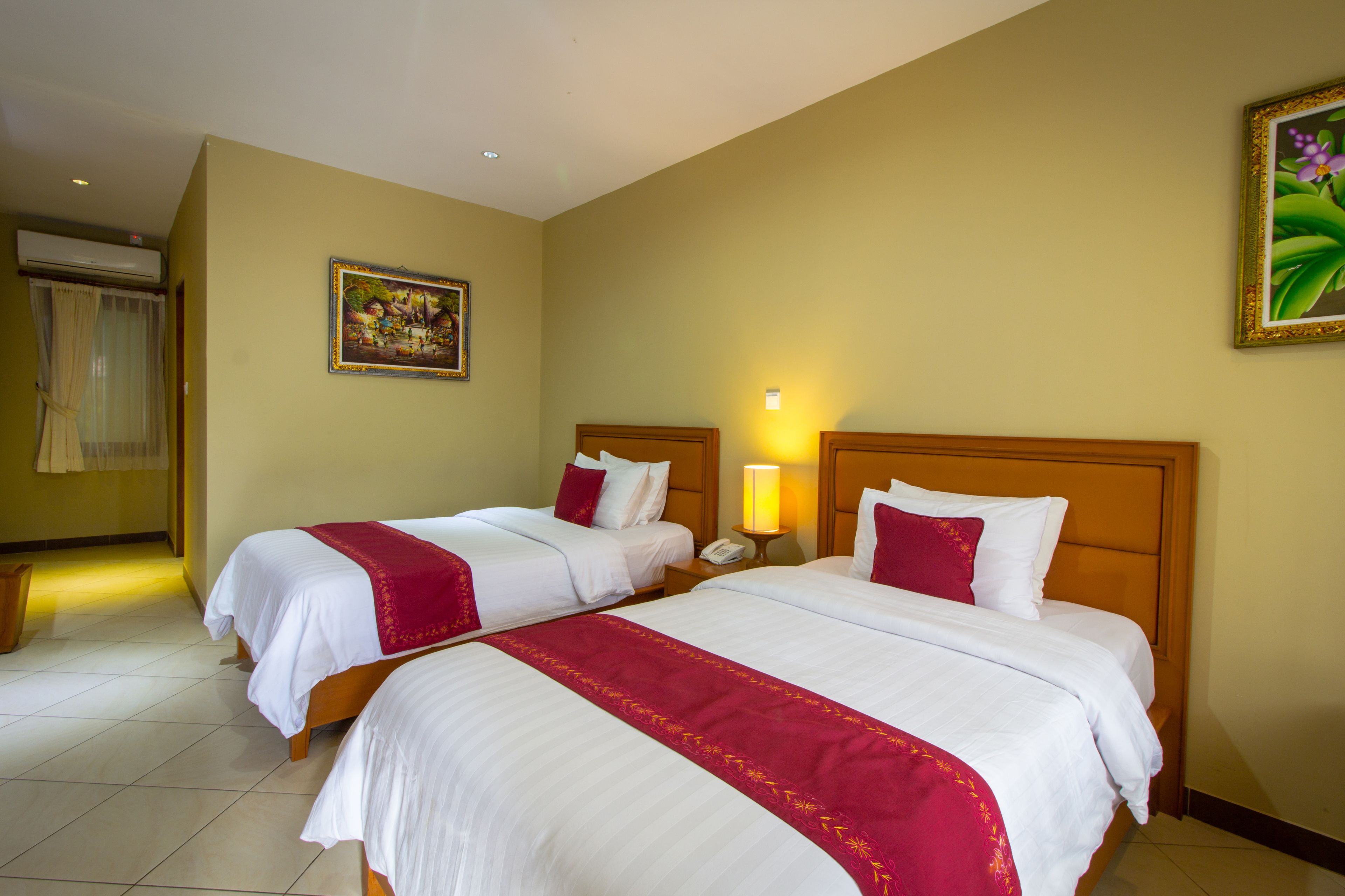 Quarto de hotel com duas camas, uma mesa de cabeceira, um abajur e um quadro na parede.