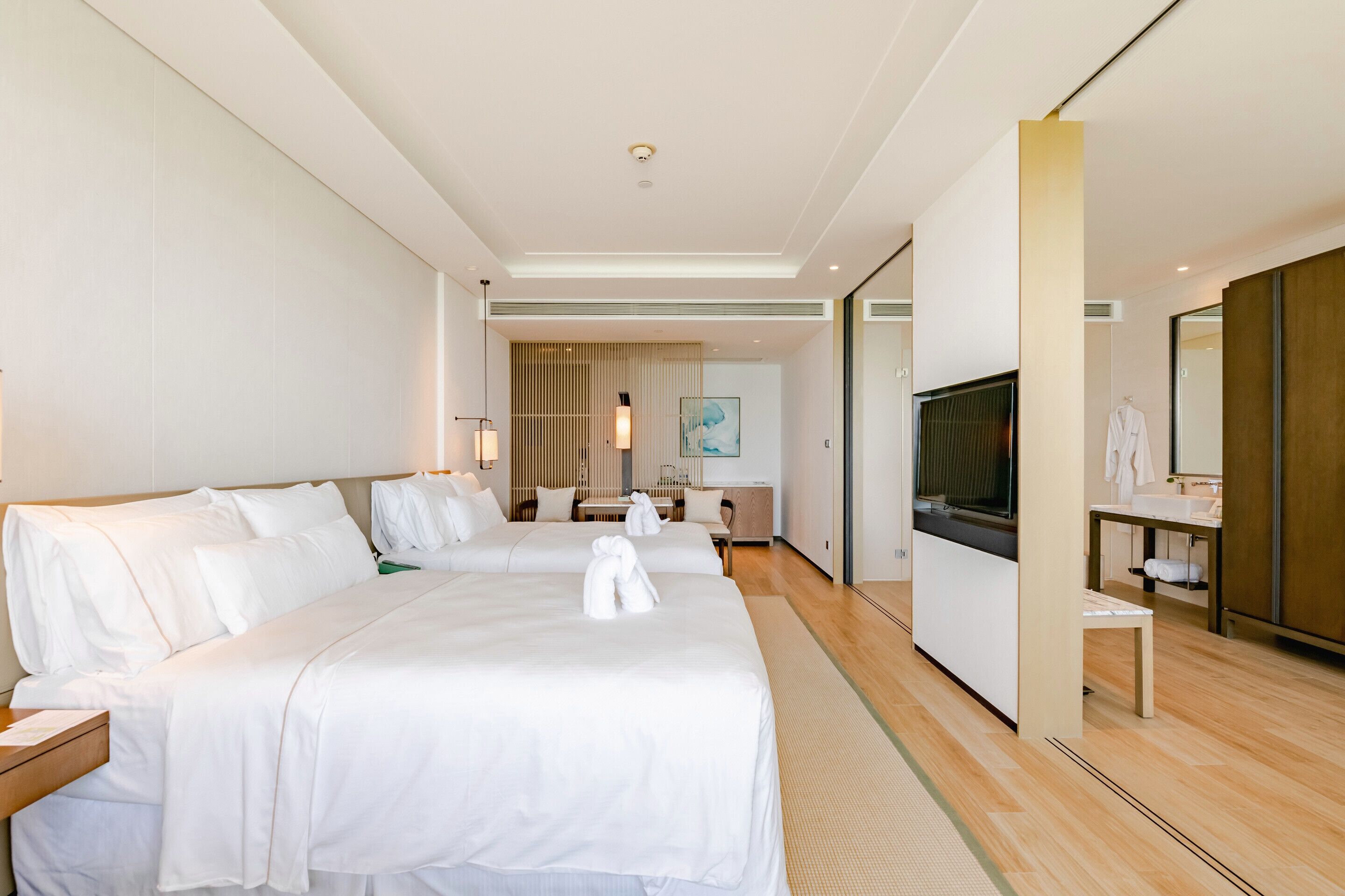 Quarto de hotel com duas camas, televisão, banheiro e área de refeições.