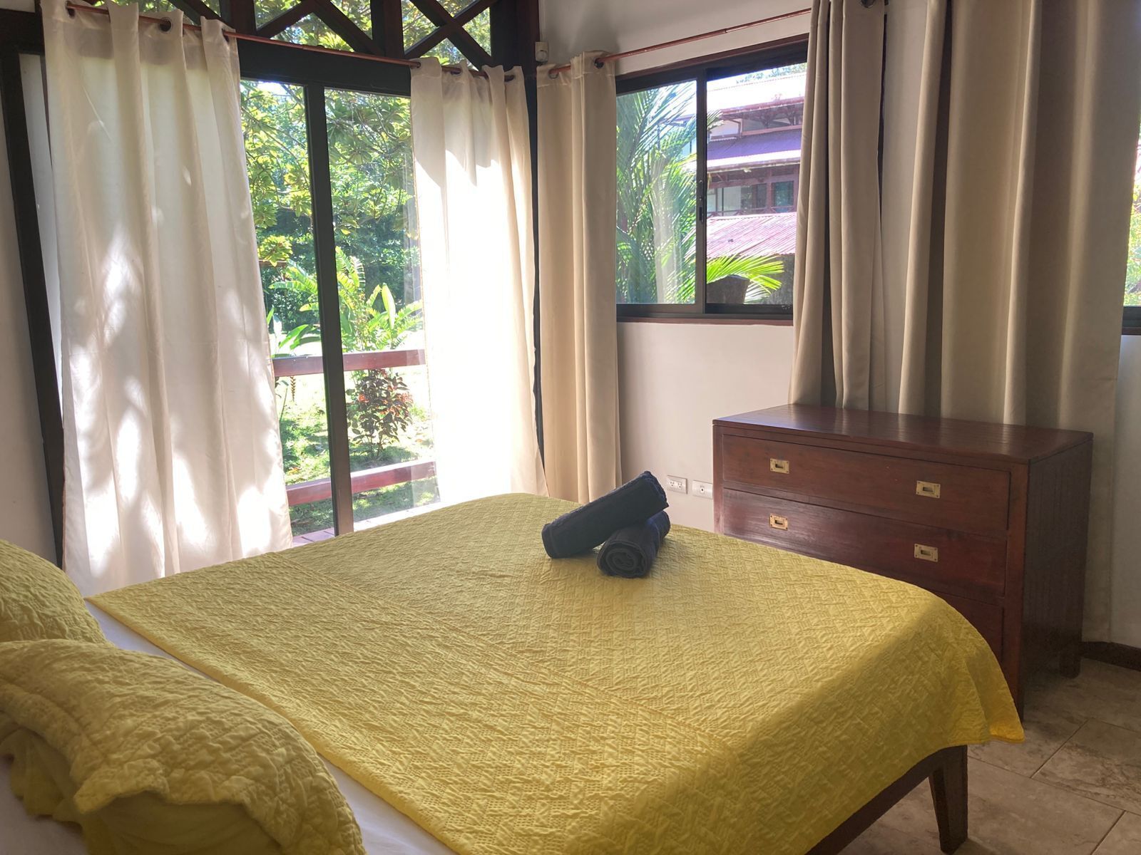 Um quarto com uma cama, uma cômoda de madeira e uma janela com cortinas.