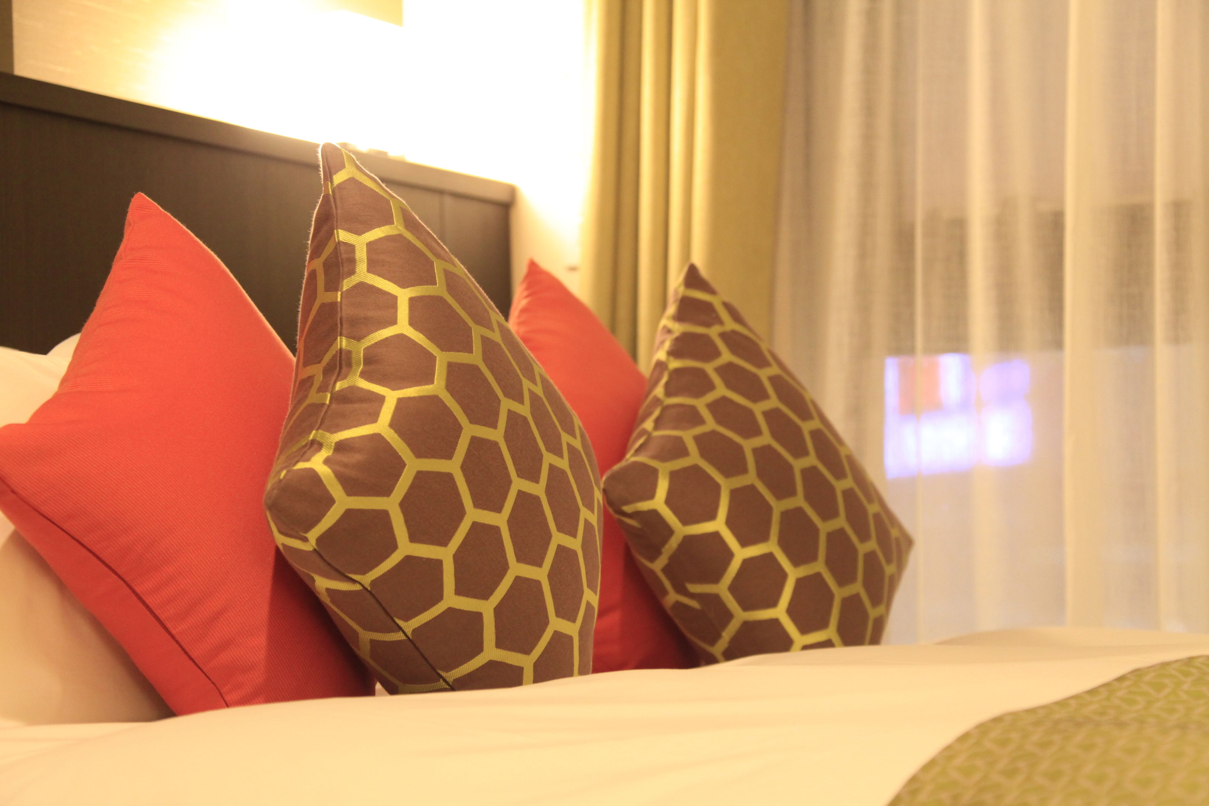 Cama com vários travesseiros, incluindo alguns vermelhos e estampados, em um quarto de hotel.