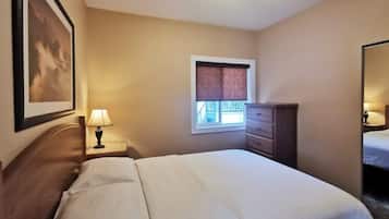 Quarto de hotel com cama, mesa de cabeceira com abajur, penteadeira, janela com persianas e um quadro na parede.