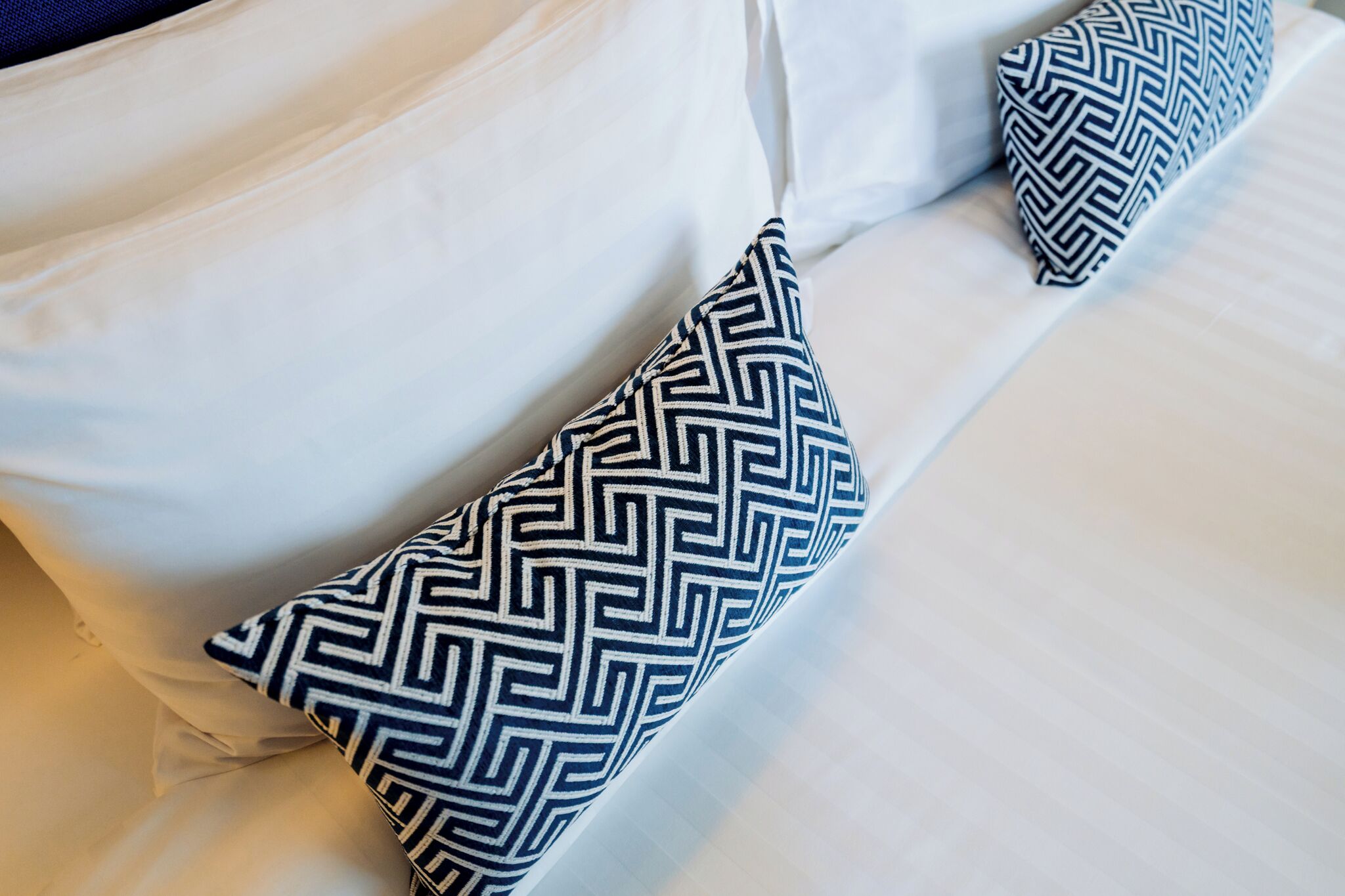 Cama com roupa de cama branca e duas almofadas com padrão geométrico preto e branco.