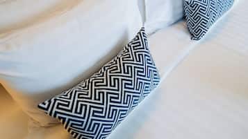Cama com roupa de cama branca e duas almofadas com padrão geométrico preto e branco.