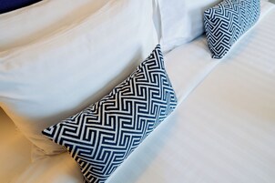 Cama com roupa de cama branca e duas almofadas com padrão geométrico preto e branco.