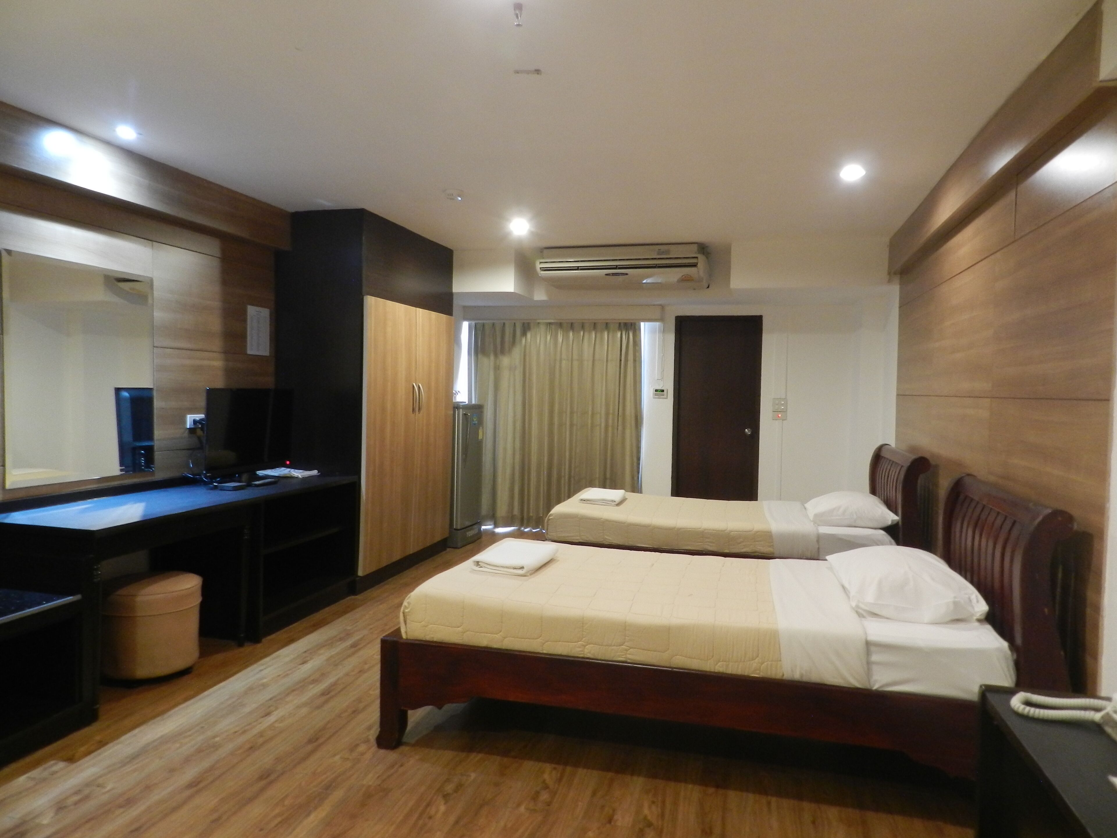 Quarto de hotel com duas camas, uma escrivaninha com computador, televisão e ar condicionado.