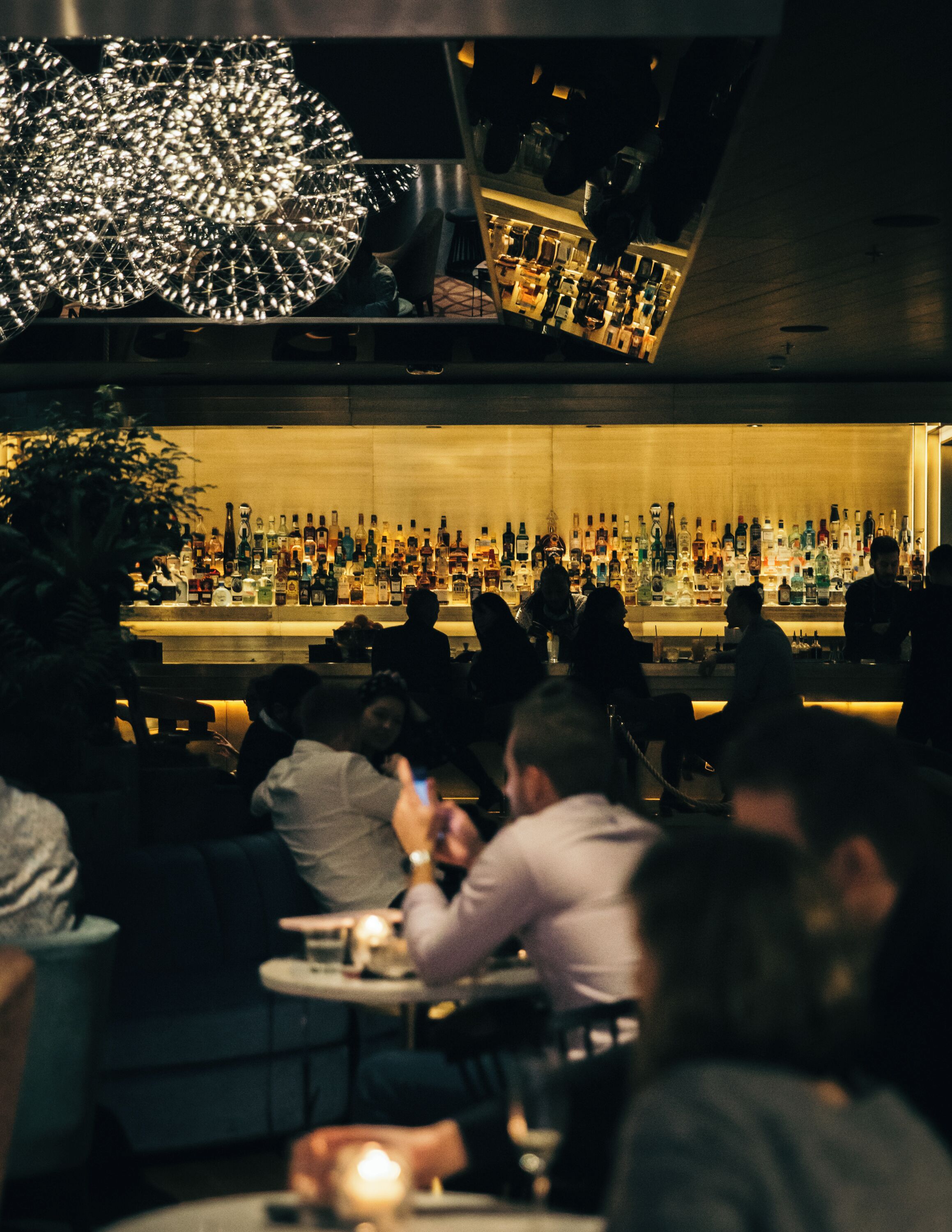 Uma área de bar com diversos tipos de garrafas e um espaço de estar com mesas e cadeiras.