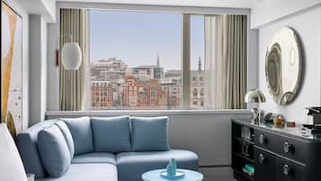 Uma sala de estar moderna com um sofá, uma mesa de centro e vista para um horizonte urbano através de amplas janelas.