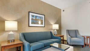 Quarto de hotel com um sofá azul, uma poltrona cinzenta, uma mesa pequena e duas luminárias.