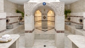 Área de spa com pisos de mármore, bancos de pedra e um arco central.