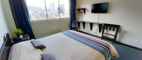 Quarto de hotel com cama grande, televisão na parede e janela com vista para a cidade.