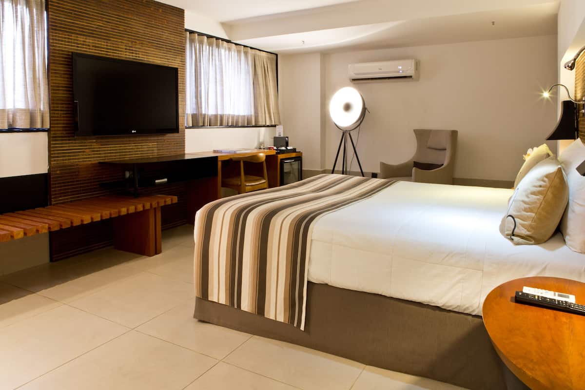 Quarto de hotel com uma cama grande, uma mesa, uma televisão, uma luminária de mesa e uma cadeira.