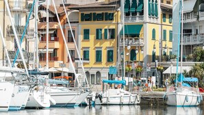 Uma marina com vários barcos atracados, um edifício amarelo com varandas e um céu claro.