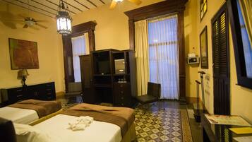 Quarto de hotel com duas camas, ventoinha no teto, televisão e um pequeno espaço para sentar.