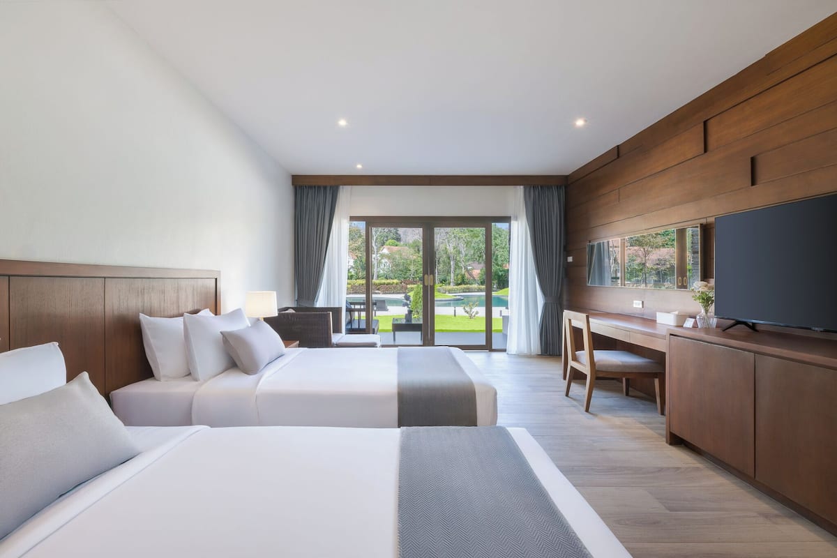 Quarto de hotel moderno com duas camas, uma escrivaninha e uma televisão.