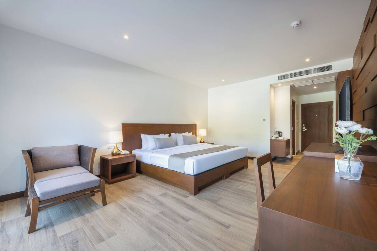 Quarto de hotel com cama, cadeira, mesa e um vaso de flores.