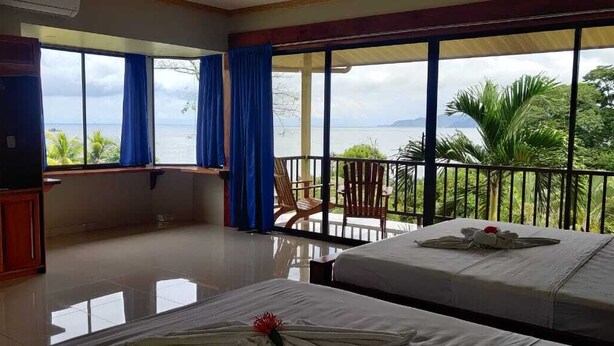 Quarto de hotel com varanda, uma cama, uma secretária e vista para o mar.