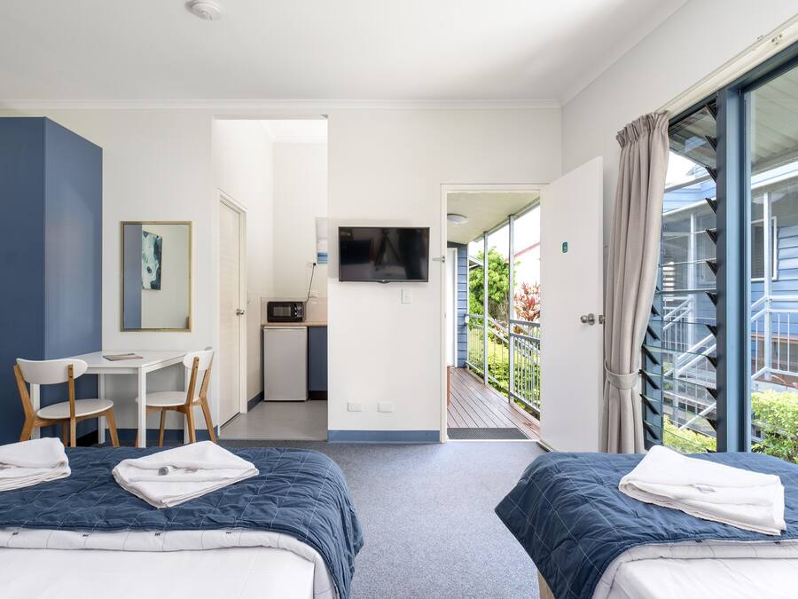 Quarto de hotel com duas camas, uma mesa, uma TV e uma varanda com vista para o exterior.