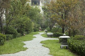 Um caminho de pedra em um jardim, com lanternas de pedra e vegetação exuberante.