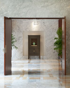 Um corredor com piso de mármore, um armário de madeira com um vaso verde e uma planta à direita.
