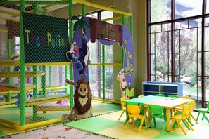 Espaço infantil com estrutura de recreação com tema de leão, mesa com cadeiras e vista para o verde lá fora.