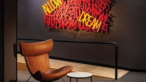 Um interior moderno com uma poltrona de couro curvada, uma pequena mesa redonda e uma parede com texto abstrato em vermelho e amarelo.